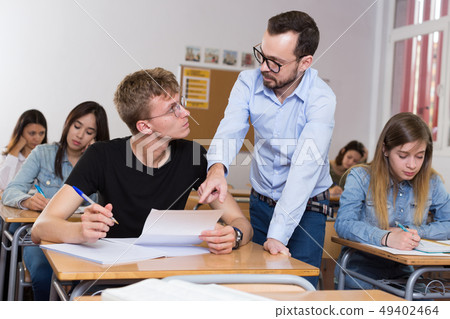 Student is writing test and answer about task and teacher is explaining ...