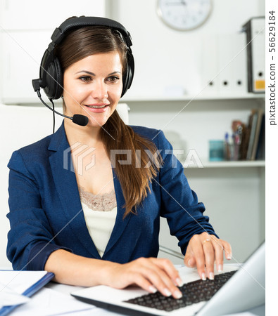 Office worker woman is working at a computer and talking by headset ...
