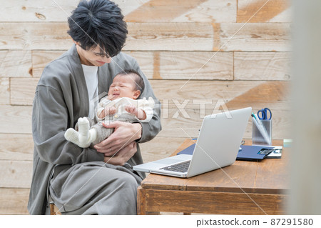 A young man holding a baby and doing remote work - Stock Photo ...