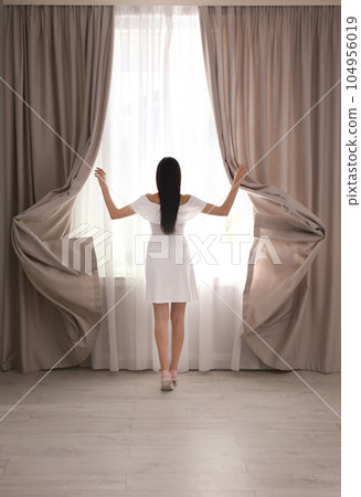 Woman opening window curtains at home in... - Stock Photo [104956019 ...