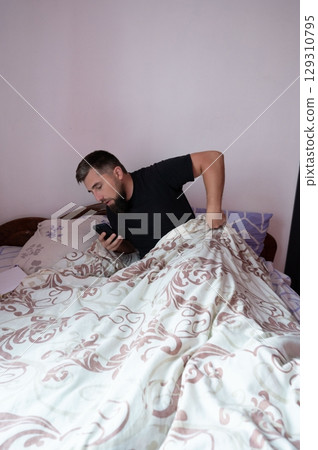 Man checks phone in bed, pulling back covers,...-照片素材（圖片） [129310795 ...