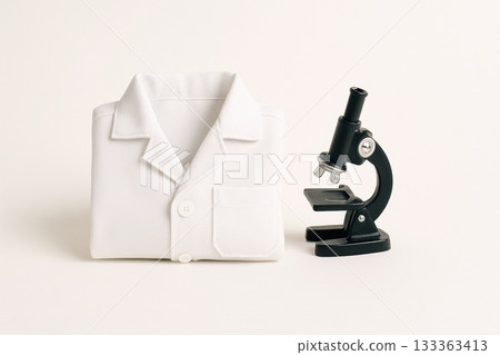 Folded white lab coat next to black microscope...-插圖素材 [133363413 ...